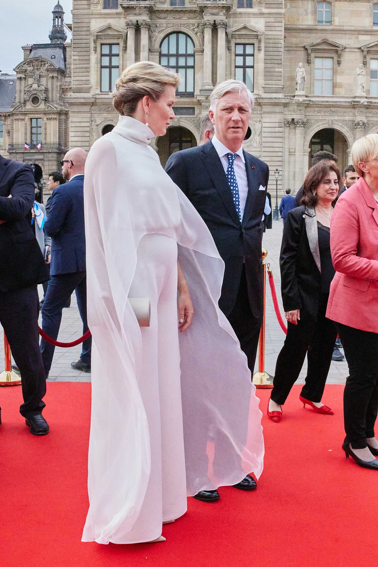 La reine Mathilde en majesté et cape au vent devant la Pyramide du Louvre