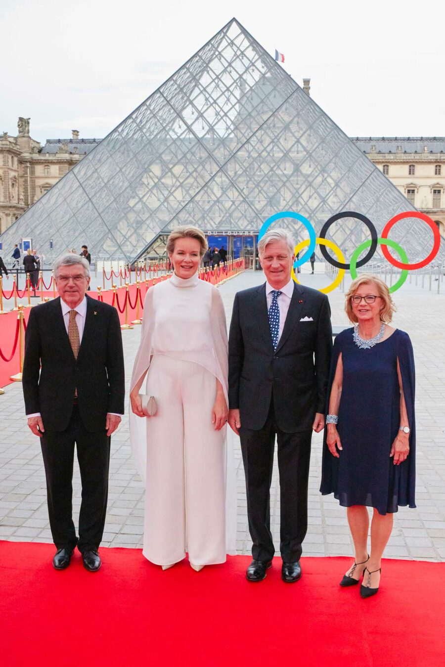 La reine Mathilde en majesté et cape au vent devant la Pyramide du Louvre